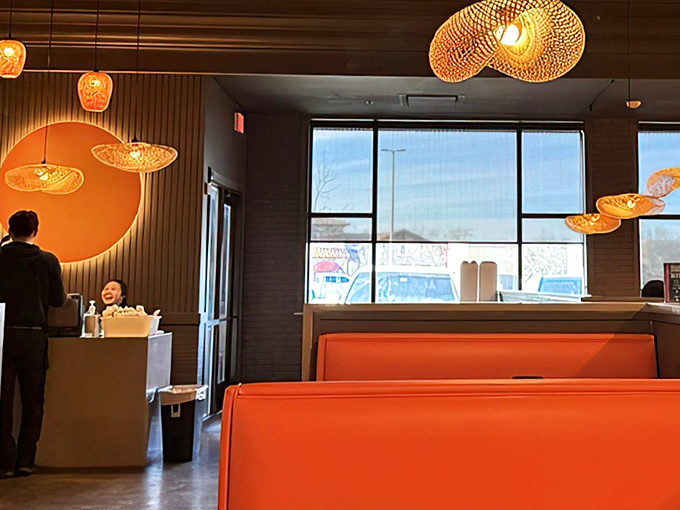 The warm glow of pendant lighting and orange booths creates an atmosphere that says, "Stay awhile, there's more food coming."