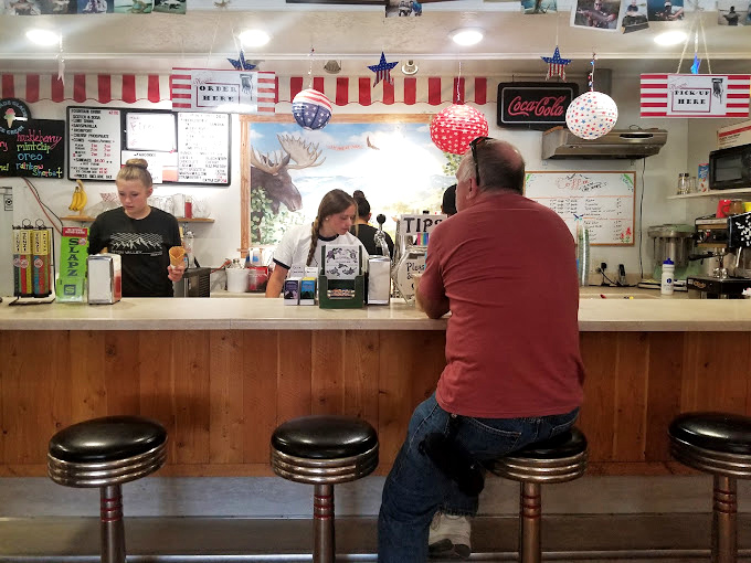 Classic diner counter with chrome stools where strangers become friends over shared purple-stained smiles and brain freeze warnings.