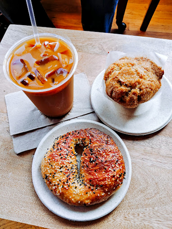The holy trinity of morning indulgence: iced coffee for survival, a perfectly seeded bagel for substance, and that muffin for pure, unadulterated joy.
