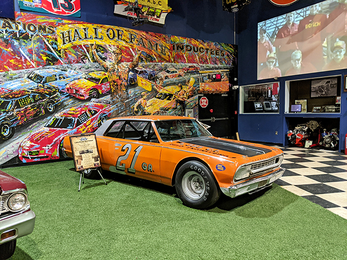 The orange #21 Chevelle sits before a vibrant mural of racing history, like an actor taking a bow against the backdrop of its greatest performance.
