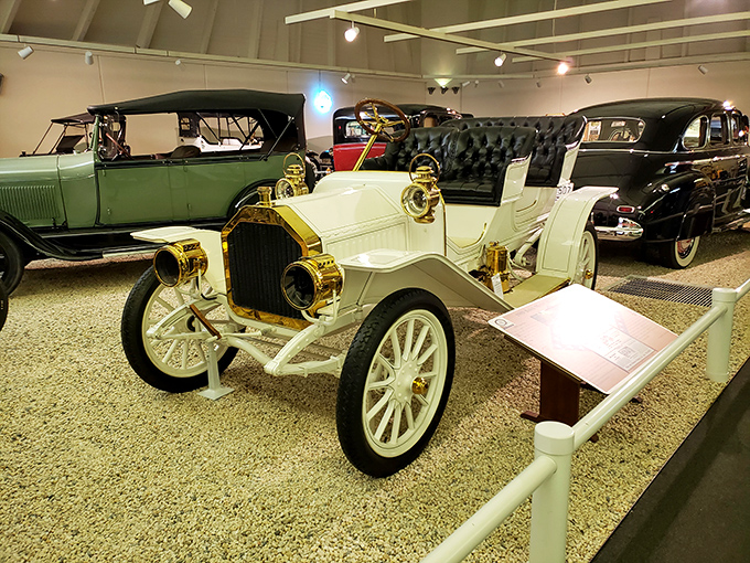 This pristine white antique Buick gleams under museum lights, its brass headlamps and hand-cranked engine recalling an era when driving was both adventure and luxury.