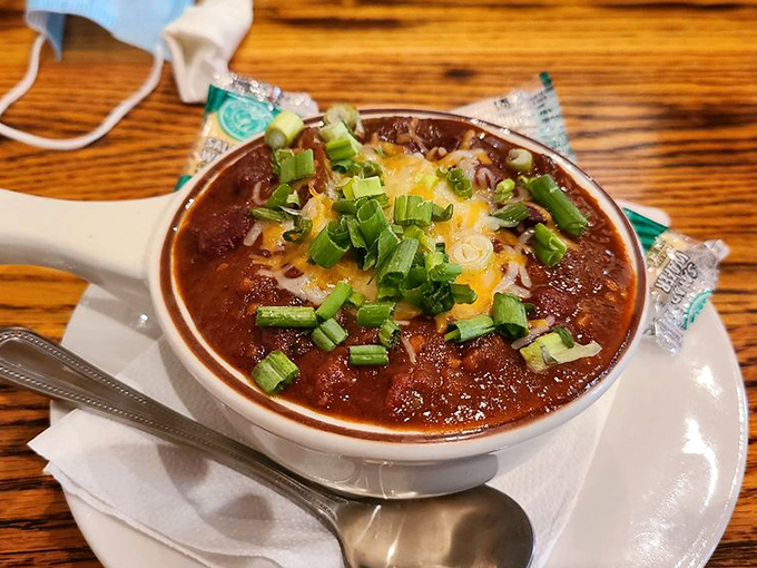 A proper bowl of chili topped with melted cheese and green onions—the kind that warms you twice: once with its heat, once with its spice.