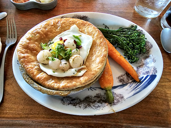 The Onion Pye arrives like a colonial surprise&mdash;a golden pastry crown revealing delicate scallops nestled in creamy sauce, with vegetables standing at attention.