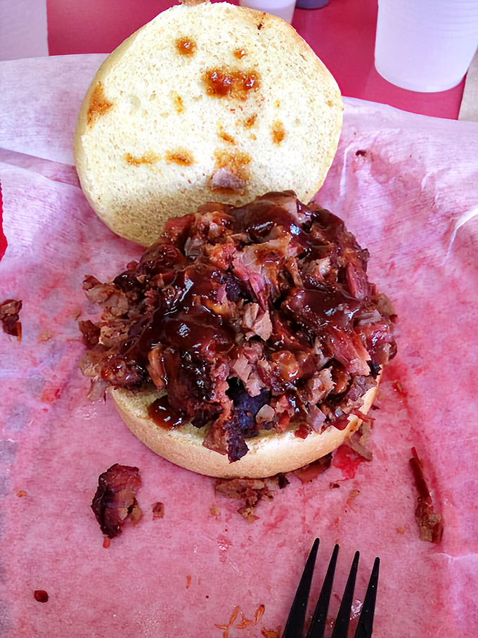 A brisket sandwich caught in its natural habitat: halfway between being assembled and devoured. That sauce-soaked meat is making a break for freedom.