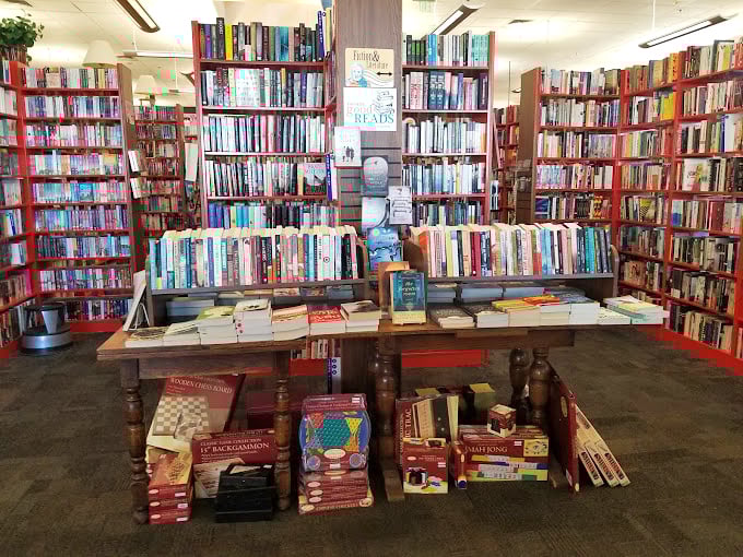 Fiction shelves create a literary fortress of solitude. That wooden table anchors the space like a library reading room without the shushing.