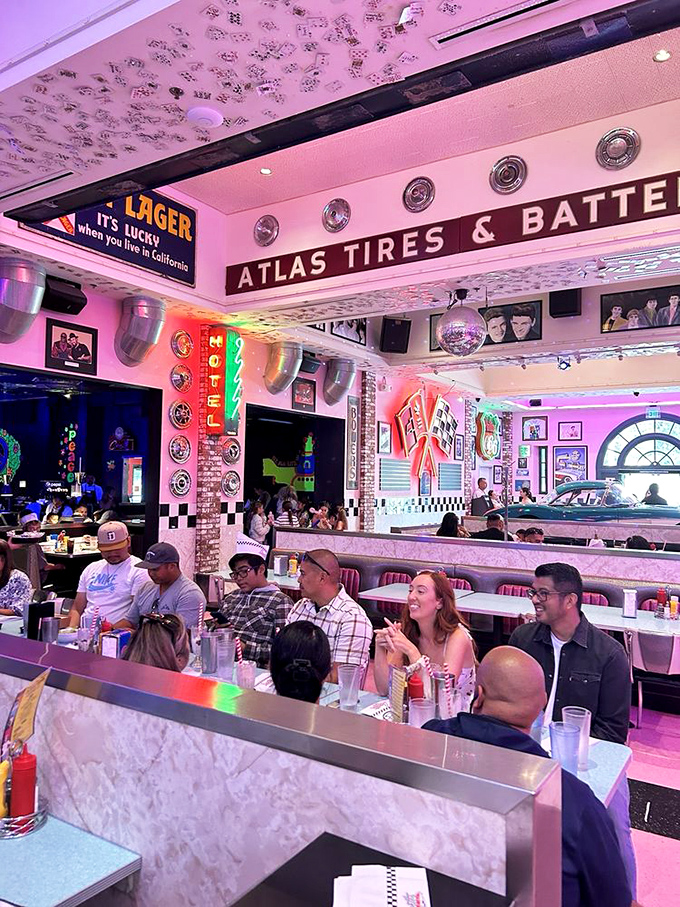 Patrons share laughter under vintage signs and pink lights, proving that good food and retro vibes are the ultimate social connectors.