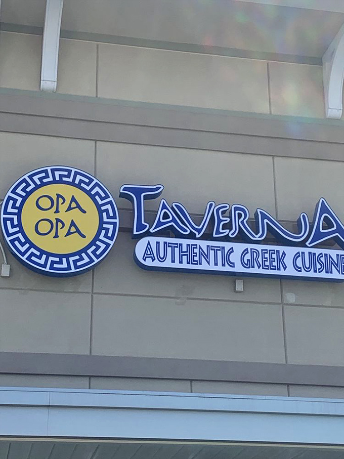 That iconic blue and yellow sign serves as a beacon for hungry souls searching for authentic Greek flavors in a sea of beach town eateries.