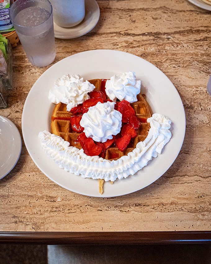 A waffle that's having more fun than you are, dressed in strawberries and whipped cream like it's headed to a breakfast gala.