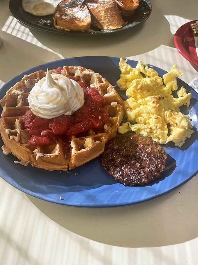 The breakfast trinity: golden waffle, fluffy scrambled eggs, and a sausage patty that didn't come from a frozen bag. Morning salvation on a blue plate.