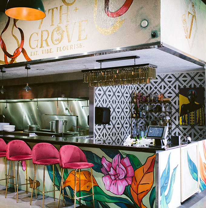 The bar area where mixology meets art, surrounded by murals that make waiting for your table feel like hanging out in a gallery with drinks.