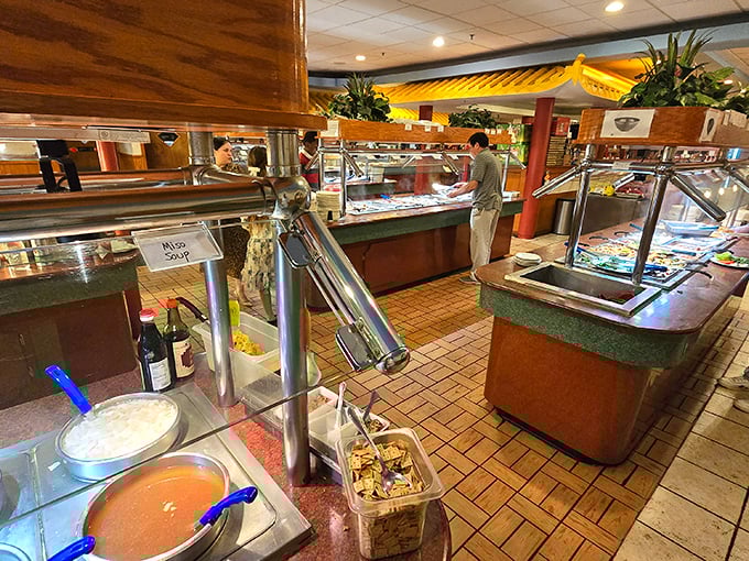 The buffet stations stand like culinary islands in a sea of possibility, each steam table a continent of flavors waiting to be explored. 