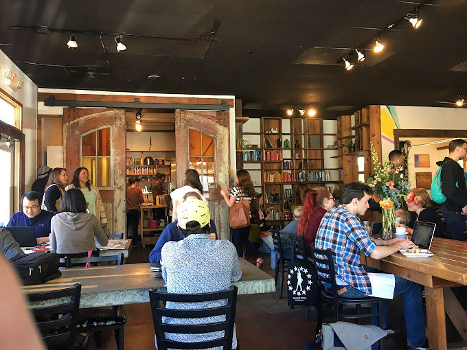 The communal tables and bookshelf doorway create that rare third space where strangers become neighbors and laptops find their natural habitat.