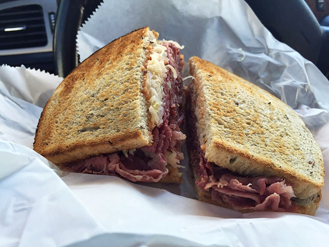The Reuben in its natural habitat—wrapped in deli paper, ready for devouring. Those perfectly toasted rye slices barely contain their corned beef bounty.