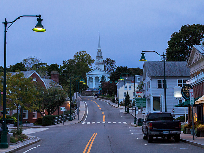 Mystic's Main Street at dusk &ndash; where the white church steeple stands like a lighthouse guiding locals home after a day of friendly encounters.