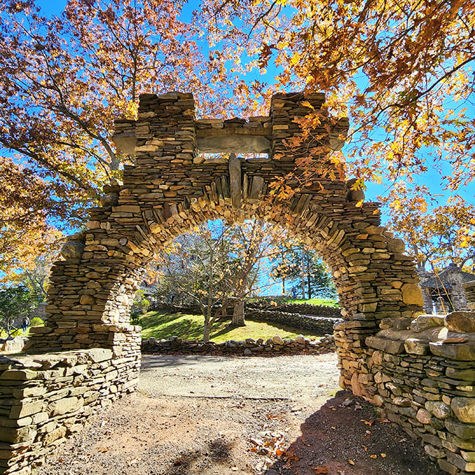 Nature frames perfection as autumn leaves dance above this masterfully crafted stone arch, inviting visitors to step through into another world entirely.