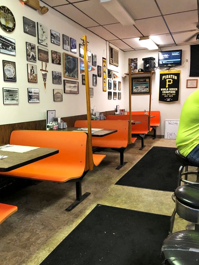 The orange booths aren't just seating—they're time machines to a simpler era when conversations happened face-to-face and Pirates memorabilia was required wall decor.