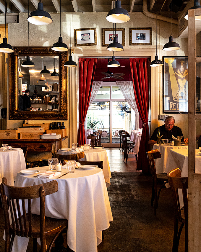 Step inside and time travel begins—rich red curtains, vintage mirrors, and pendant lights create the kind of bistro ambiance that makes conversations better and memories longer.