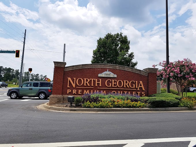 The grand entrance sign, surrounded by seasonal blooms, stands as a retail promised land for bargain hunters across Georgia.
