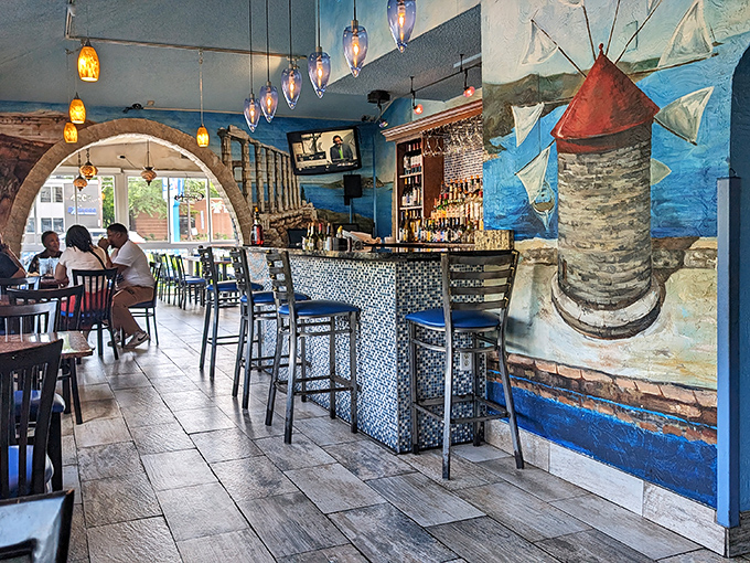 Inside, Mediterranean blue walls and windmill murals transport you straight to the Aegean. The mosaic bar beckons with promises of ouzo.