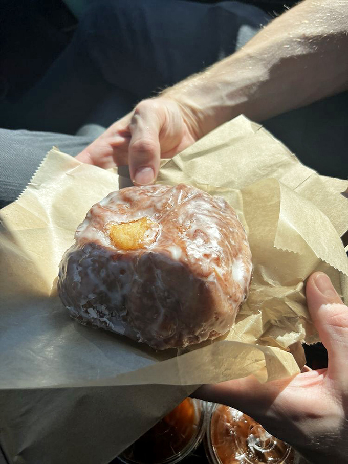 That glistening apple fritter, still warm and cradled in parchment, represents everything right with American breakfast culture.