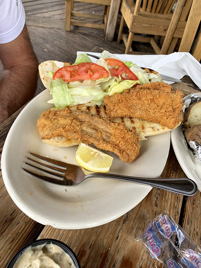 The fish sandwich arrives like seafood royalty on a throne of lettuce and tomato, with golden-fried perfection that makes you want to applaud.