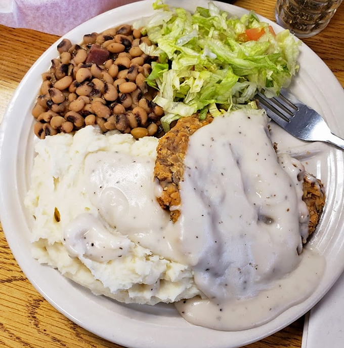 The legendary chicken fried steak in its natural habitat &ndash; swimming in gravy with faithful sidekicks of mashed potatoes, black-eyed peas, and salad. 