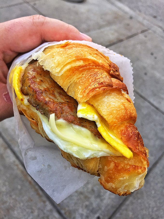 Breakfast sandwich perfection: a golden croissant cradling eggs and sausage &ndash; proof that sometimes the best Franco-American relations happen between bread layers. 