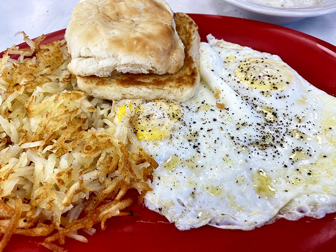 Sunny-side eggs with perfectly crispy hash browns and a biscuit that could make your grandma jealous. Breakfast nirvana on a red plate.