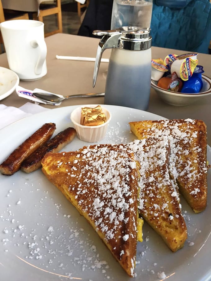 Golden-brown French toast dusted with powdered sugar sits beside perfectly caramelized sausage links &ndash; breakfast architecture at its finest.