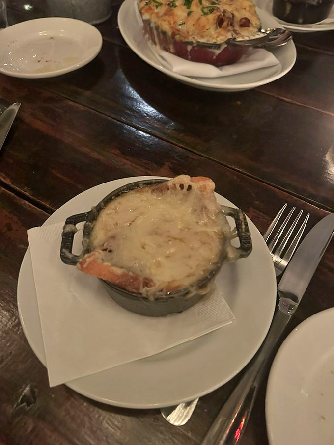 The hero has arrived! French onion soup in its cast-iron cocoon, crowned with a magnificent cheese cap that stretches with each spoonful.