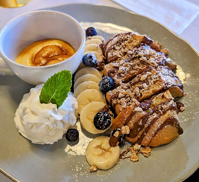 French toast nirvana achieved: thick-cut bread crowned with fresh berries, banana slices, and a side of pure maple syrup bliss.