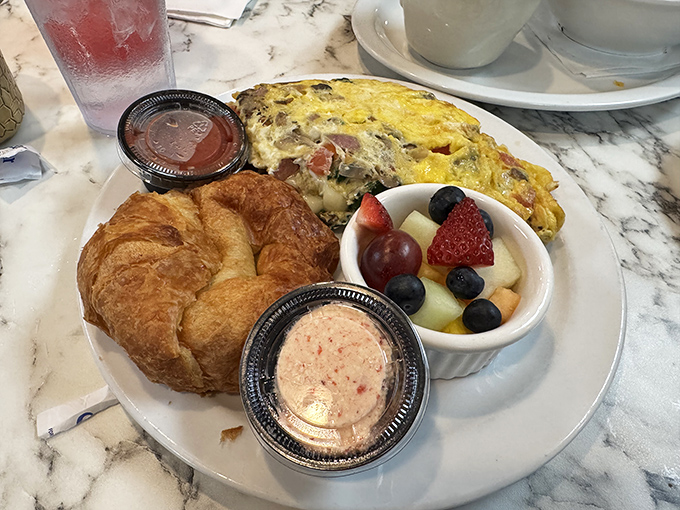 Eggs Benedict perfection – two golden-domed poached eggs perched atop Canadian bacon, draped in hollandaise that cascades like a yellow waterfall.