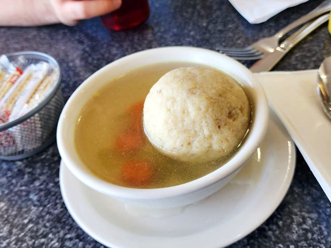 Golden broth cradling a perfect matzo ball &ndash; this isn't just soup, it's liquid sunshine with a dumpling island of joy.