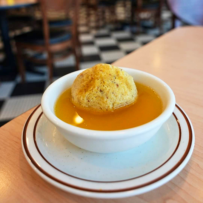That golden matzo ball floating like a perfect edible moon in chicken broth so clear you could read yesterday's Tribune through it.