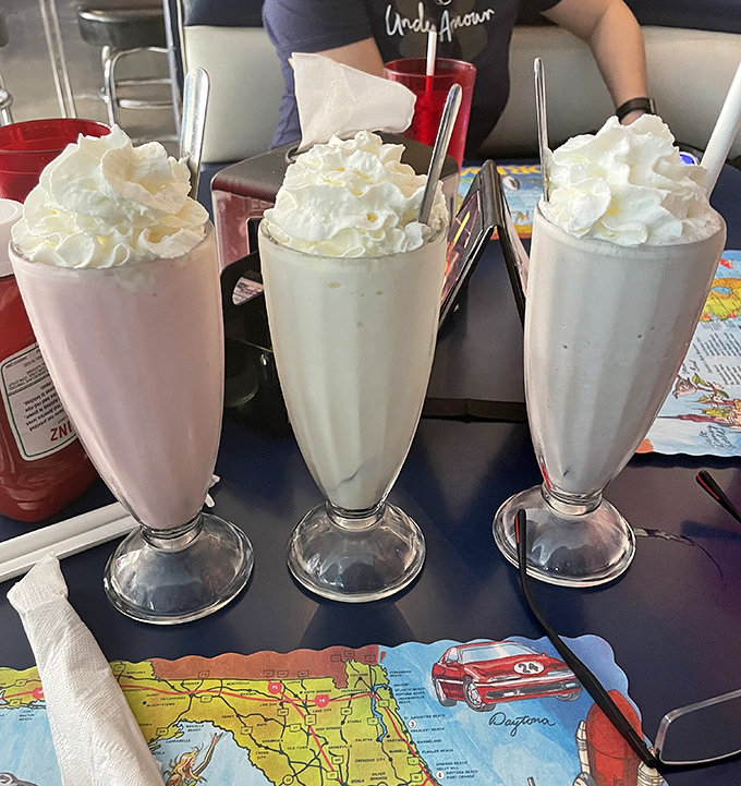 Three milkshakes standing tall like the Three Tenors of dairy—each topped with a cloud of whipped cream that demands a moment of reverent silence before diving in.