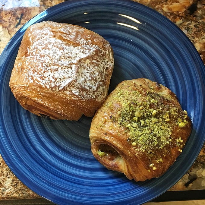 Two pastry soulmates sharing a blue plate: one dusted with powdered sugar, the other flaunting pistachio crumbles like edible emeralds.