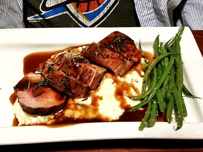 The pork tenderloin arrives like a perfectly composed still life – pink-centered medallions resting on creamy mashed potatoes with green beans standing at attention.
