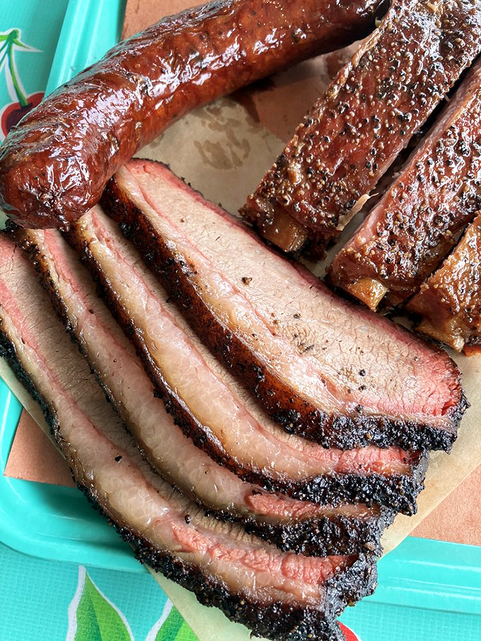 Behold the holy grail of barbecue: perfectly sliced brisket with that textbook smoke ring and bark that would make a Texan weep with joy.
