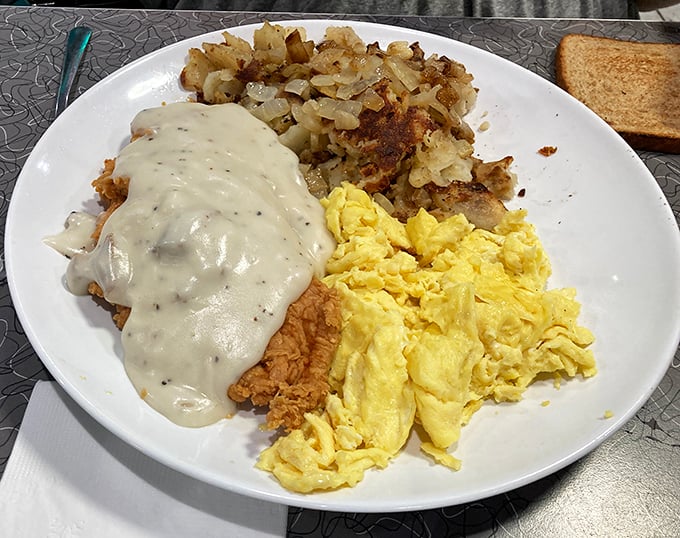 Behold the holy trinity of breakfast perfection: golden chicken fried steak smothered in creamy gravy, fluffy scrambled eggs, and crispy hash browns that demand your immediate attention.