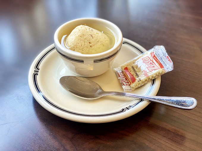 The matzo ball floats majestically in golden broth like the moon in a chicken-flavored sky, accompanied by its faithful sidekick, the saltine.