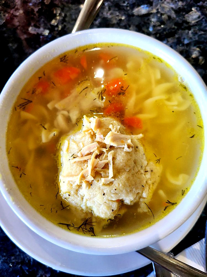 Behold the star attraction: a matzo ball floating majestically in golden broth like the moon in a chicken-flavored galaxy.
