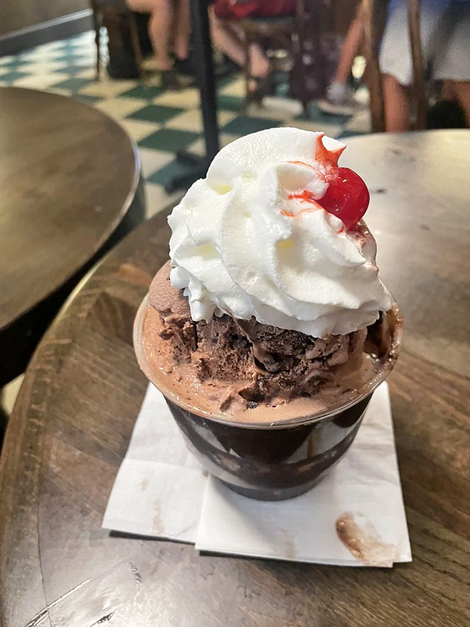 This isn't just a hot fudge sundae; it's architecture in dessert form, with that perfect cherry sentinel standing guard atop a cloud of whipped cream.