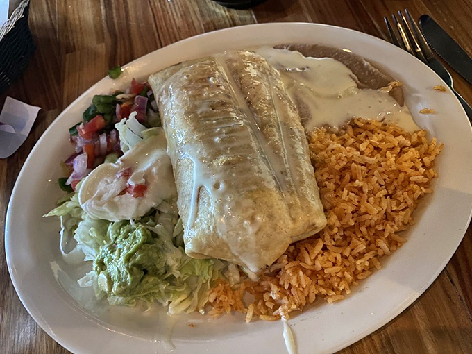 The chicken chimichanga arrives like royalty, draped in velvety cheese sauce and surrounded by its loyal court of rice, lettuce, and guacamole.