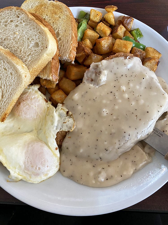 The holy trinity of breakfast: perfectly cooked eggs, golden toast, and country-fried steak swimming in peppery gravy that would make your grandma proud.