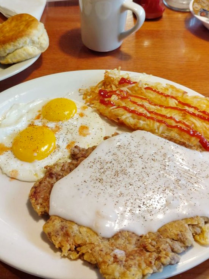 Breakfast of champions! Chicken fried steak crowned with peppery gravy, sunny-side-up eggs, and hash browns drizzled with ketchup &ndash; a morning masterpiece.
