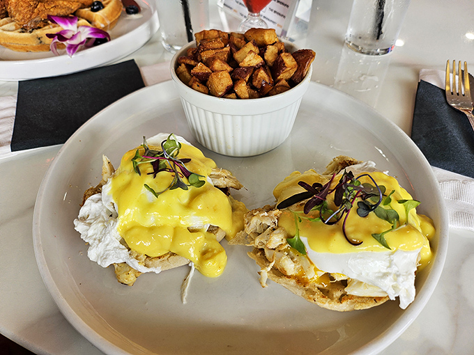 Eggs Benedict reimagined with a golden hollandaise waterfall cascading over perfectly poached eggs. Poetry on a plate with home fries.