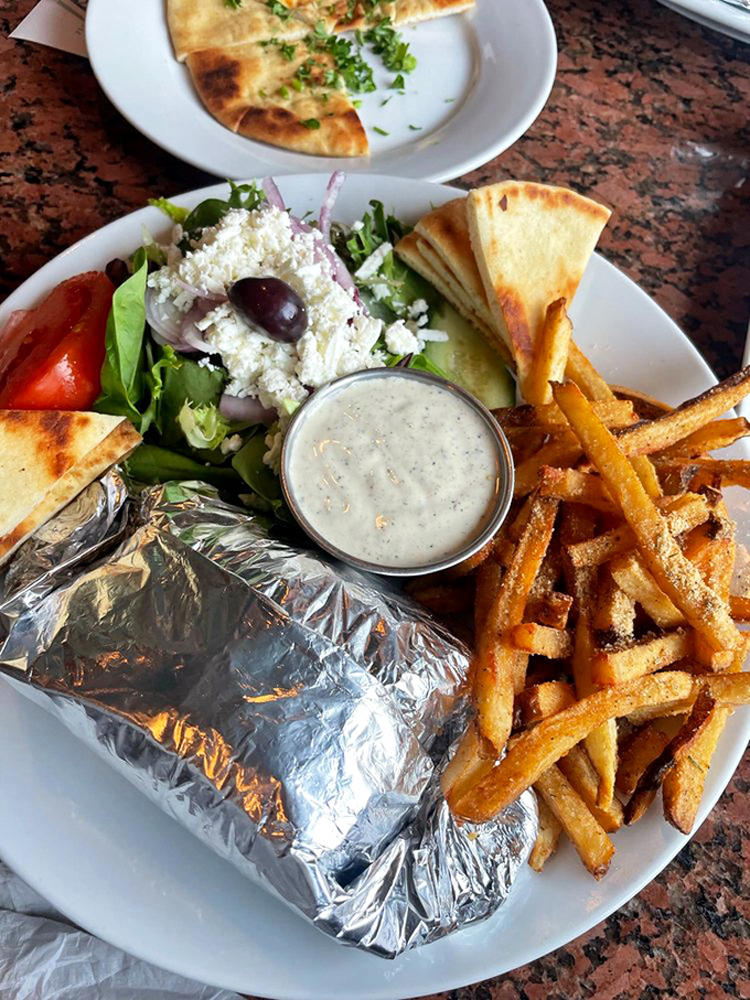 Not just a meal, but a Mediterranean vacation on a plate. The Greek salad, fries, and foil-wrapped gyro form a holy trinity.