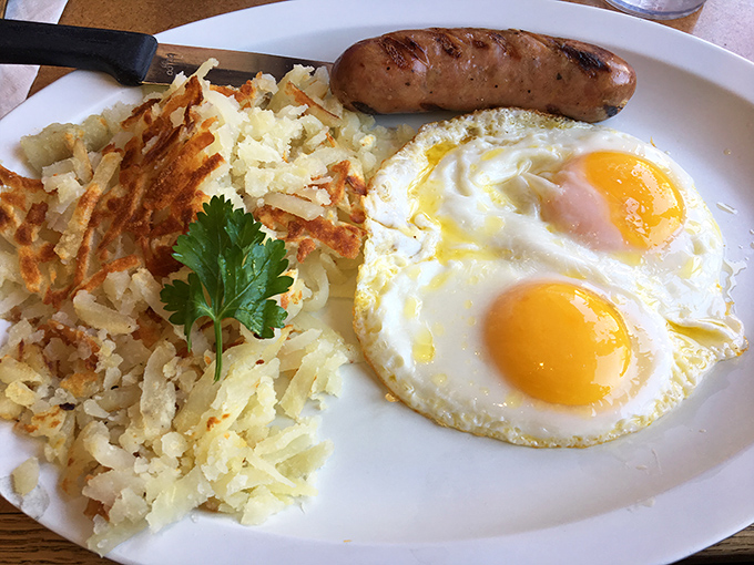 The holy trinity of breakfast: perfectly sunny eggs, a sausage link with snap, and those legendary hash browns that justify the journey. 