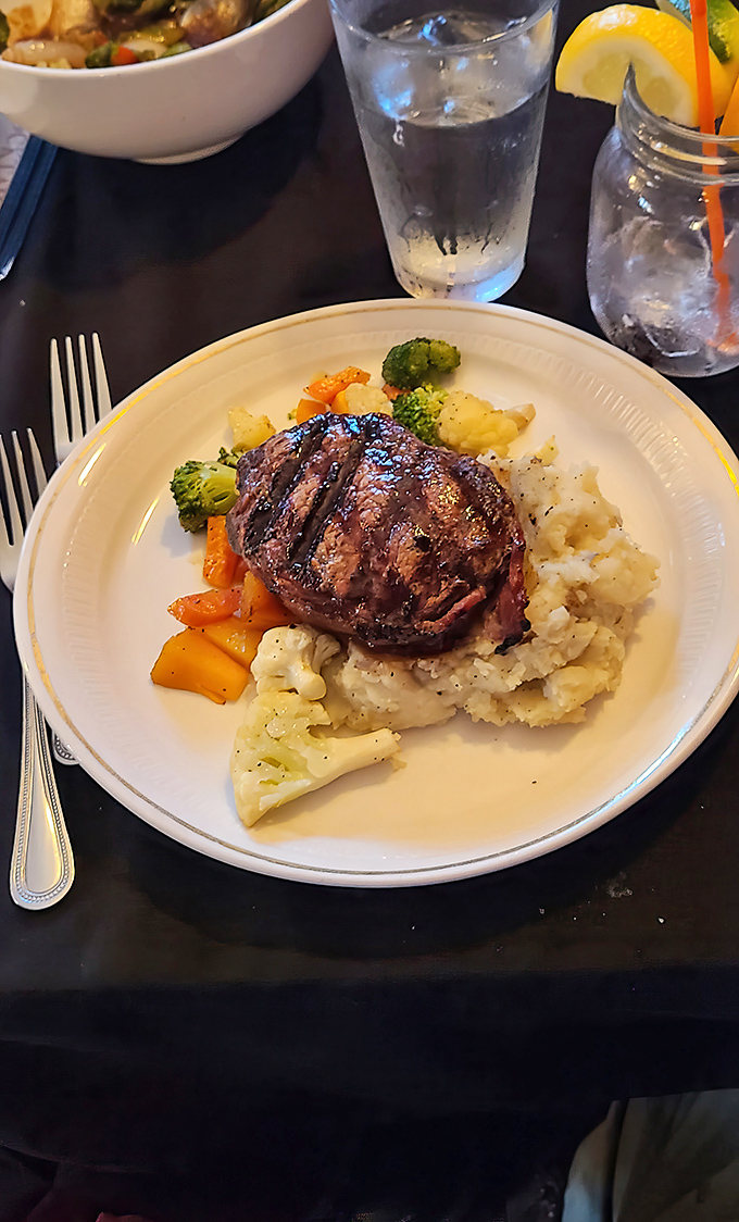 Steak perfection doesn't happen by accident. This masterpiece sits atop mashed potatoes with colorful vegetables, creating the holy trinity of Midwestern culinary bliss.