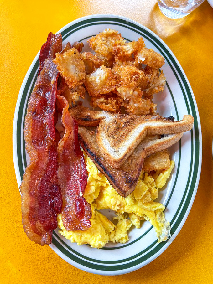The holy trinity of breakfast perfection: crispy bacon, fluffy scrambled eggs, and golden hash browns that crunch like autumn leaves.